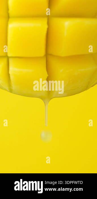 Mango juice slowly dripping from fresh fruit, yellow background ...