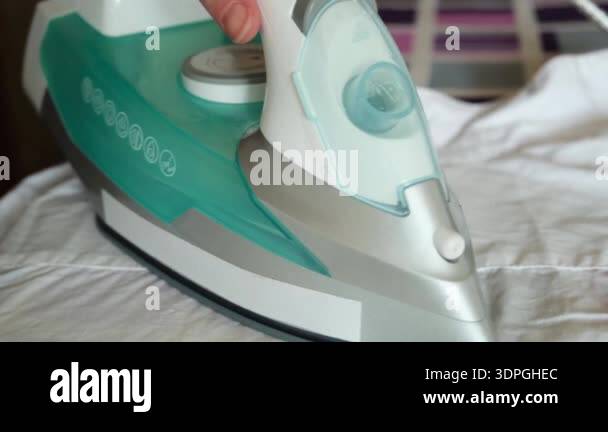 Female hand holding electric iron ironing clothes on ironing board ...