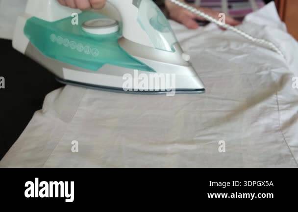 Female hand holding electric iron ironing clothes on ironing board ...