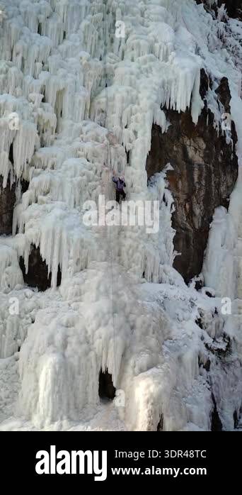 Ice climber ascending frozen waterfall with icicles on rocky cliff in ...