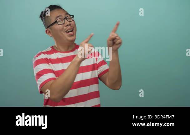 Young chinese man smiling and pointing both index fingers in studio ...