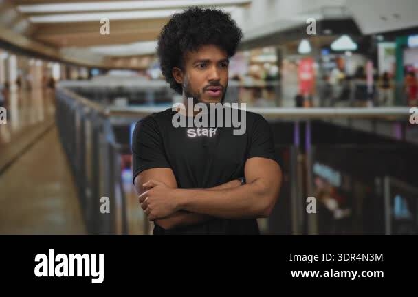 Man wearing a staff uniform stands with arms crossed in an indoor art ...