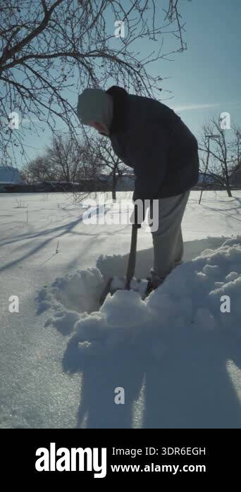 A person shovels snow in a winter field. The sun shines in the sky as ...