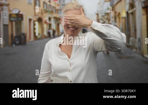 Woman middle aged smiling with hand covering eyes on a city street ...