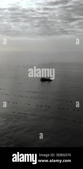 lonely boat drifting in monochrome ocean with low clouds and faint ...