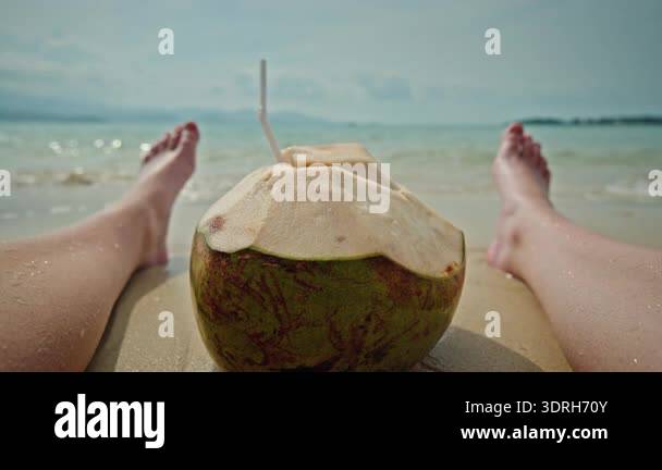 Young woman relaxing on sandy beach with green coconut and straw ...