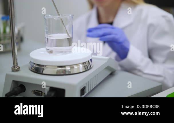 Female researcher monitoring solution mixing on magnetic stirrer ...