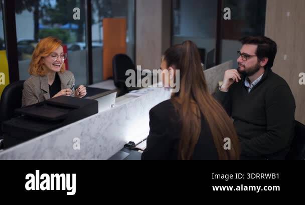 Two individuals are engaged in a conversation at a reception desk. They ...