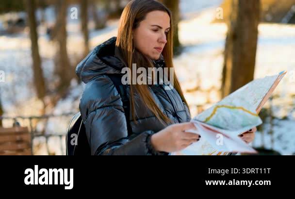 A woman in a winter coat studies a map in a snowy forest. The scene ...