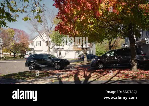 Quiet suburban neighborhood with parked cars and colorful autumn trees ...