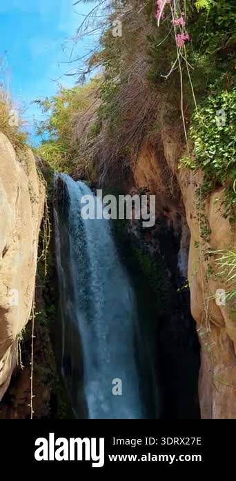 Small waterfall cascading between rocky cliffs under blue sky. Natural ...
