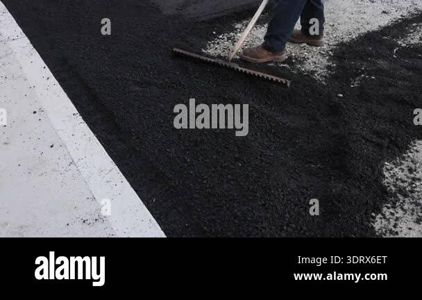 Worker uses rake to level freshly laid asphalt on road process takes ...