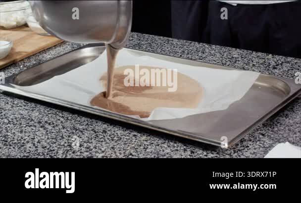 Baker pours liquid chocolate cake batter onto metal oven-tray with ...