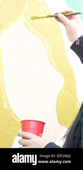Close-up of a hand using a paintbrush to fill in a yellow mural of a ...