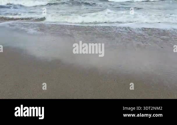 Close-up view of foamy ocean waves receding from a sandy beach ...