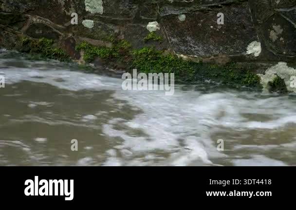 Fast flowing mountain river along moss covered stone embankment ...