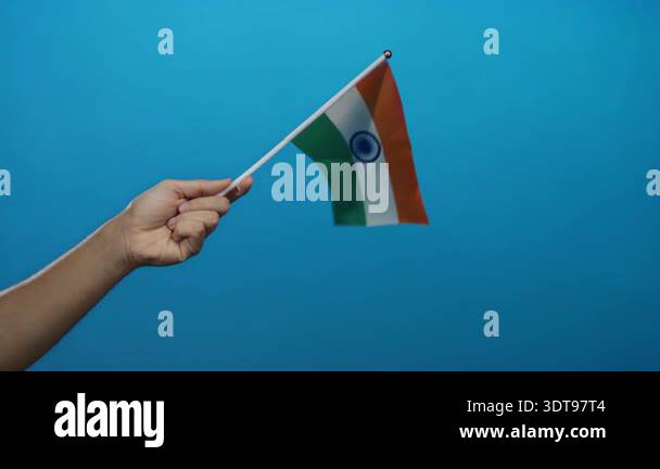Hand of a man holding indian flag against blue background, symbolizing ...