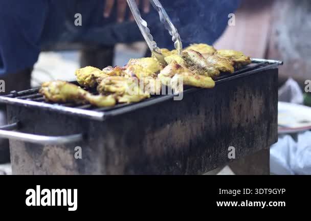 A person is basting marinated fish on a charcoal grill using a ...