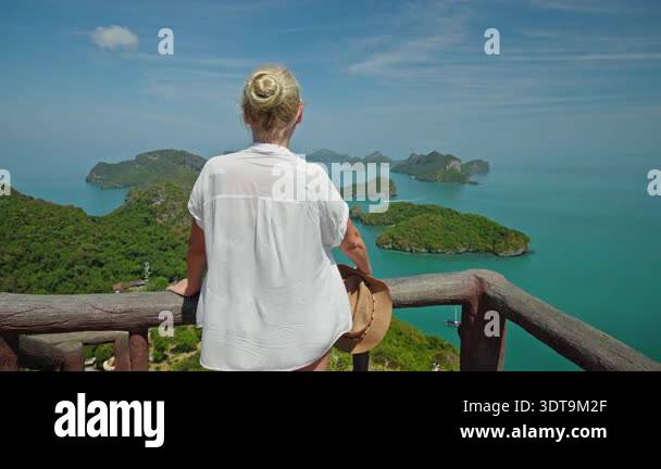 Middle-aged woman standing at a panoramic viewpoint, holding a straw ...