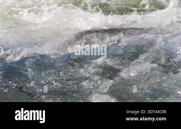 Water flowing over rocks in shallow river forming white waves, slow ...