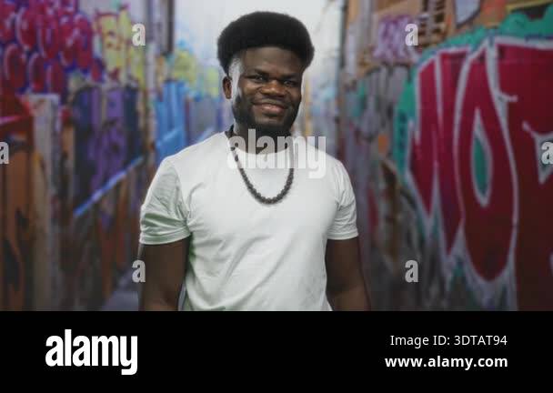 Man wearing white t shirt and beaded necklace smiles with hands on hips ...