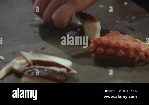 A chef slices cooked octopus tentacles on a cutting board. The chef's ...
