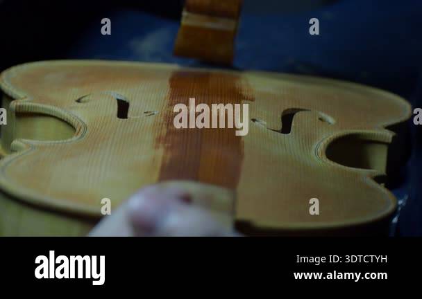 Luthier hands brushing golden amber varnish onto a violin back plate ...