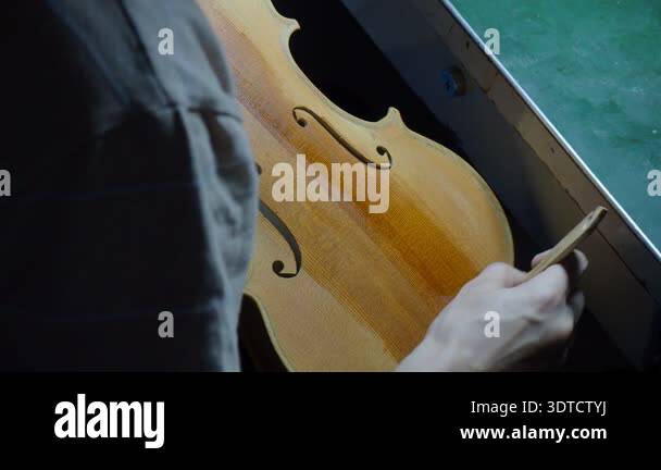 Luthier hands brushing golden amber varnish onto a violin back plate ...