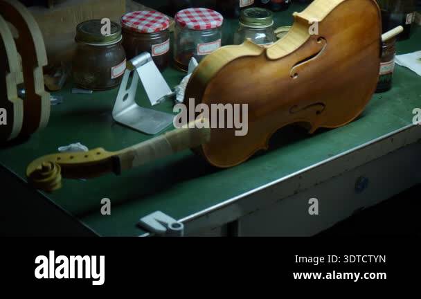 Luthier hands brushing golden amber varnish onto a violin back plate ...