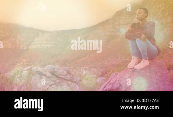 Woman crouching on boulder as rising sun creating animated light flares ...