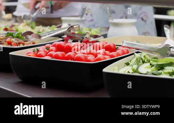 Tomatoes at a buffet next to other vegetables and salad on a table ...