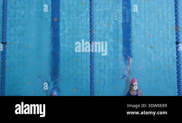 Two female swimmers pushing off pool wall and performing backstroke ...