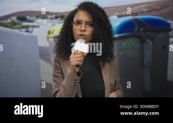 Woman reporter holding microphone in front of recycling containers on ...