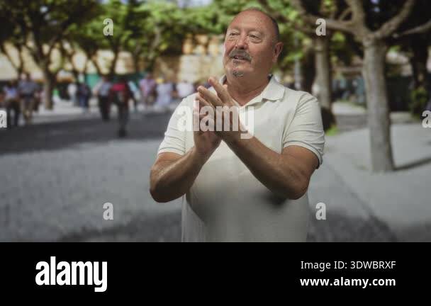 Man clapping hands on a tree lined street, wearing a white polo and ...