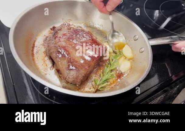 Close up of beef steak searing in stainless steel pan with garlic ...
