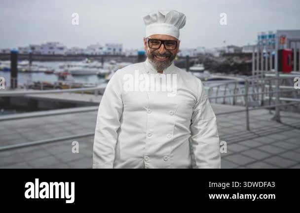Man chef in white uniform and hat smiling with visible face and beard ...