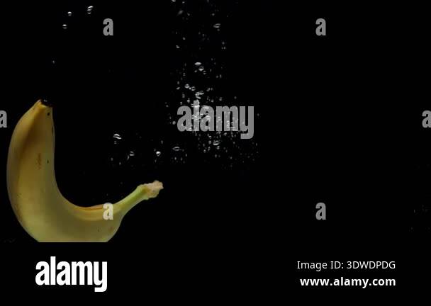 Slow motion one banana falling into transparent water on black ...