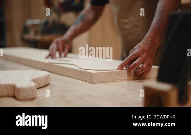 Hands of a craftsman with tattoos positioning a paper pattern on wood ...
