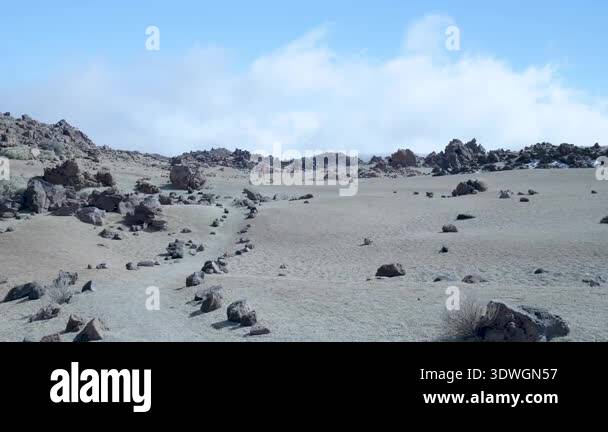 Hikers walk along a rocky path in a vast volcanic landscape under a ...