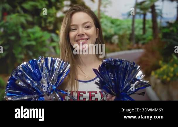 Cheerleader woman holds blue and silver pom poms while smiling and ...