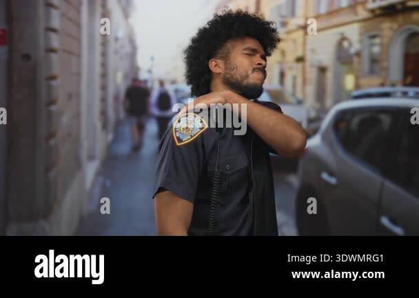 Police officer with curly hair grimaces in pain while holding his ...