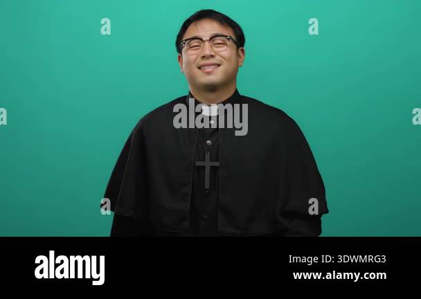 Smiling priest with glasses in black robe and cross necklace against ...