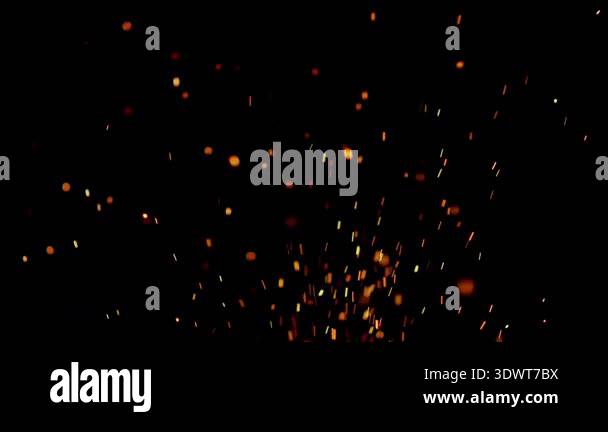 Burning orange embers and sparks flying upwards against a black ...