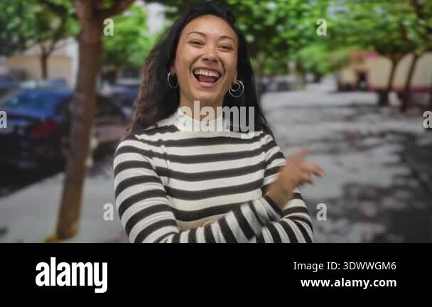 Woman points finger to cheek and sticks tongue out on a street with ...