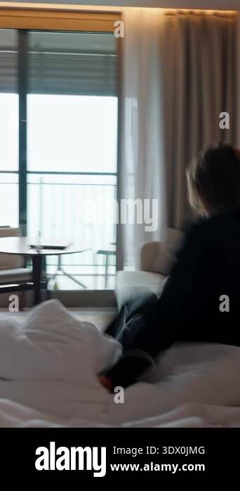 Woman standing in a modern hotel room after waking up, holding her head ...
