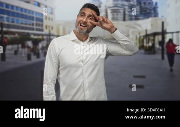 Man showing v sign by eye with visible hand on a city street, smiling ...