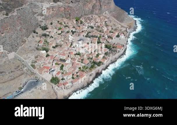 Drone view of a stone seaside village built beneath a towering rock ...