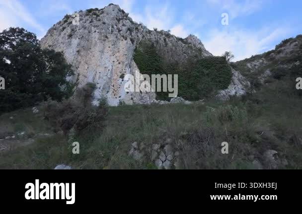 A still mountain scene with a limestone cliff and trees, where thin ...