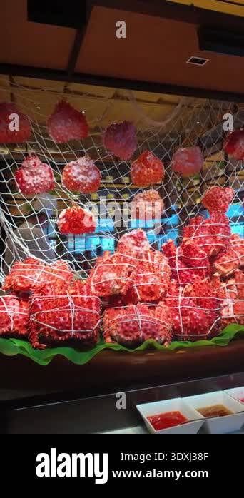 Red crabs are piled high on green leaves behind fishing net, with ...