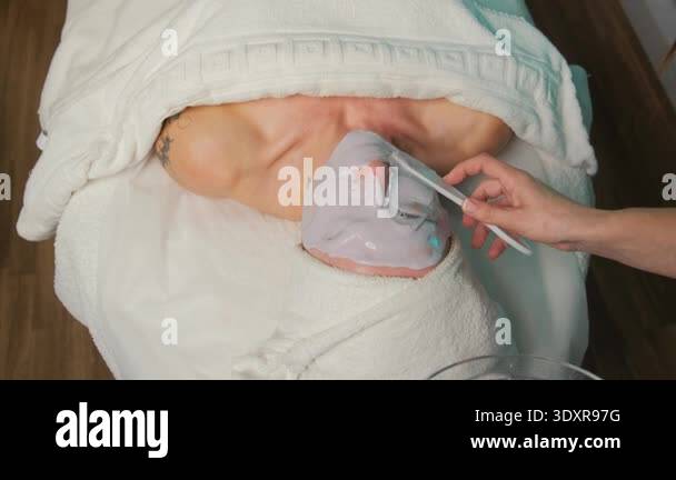 Professional beautician applying a purple alginate peel-off mask to a ...